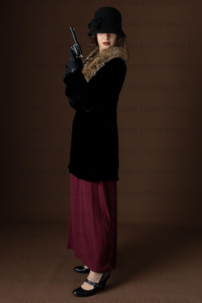 1920s woman holding a gun and wearing a black velvet coat and cloche h ...